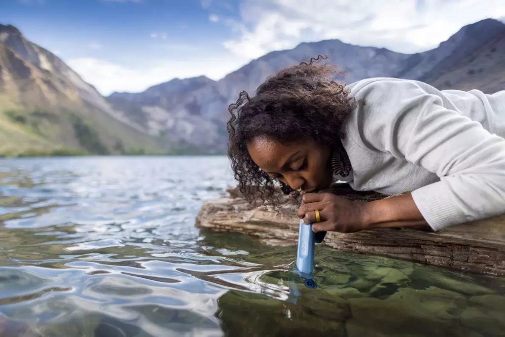 kvinna som använder lifestraw för att dricka från floden