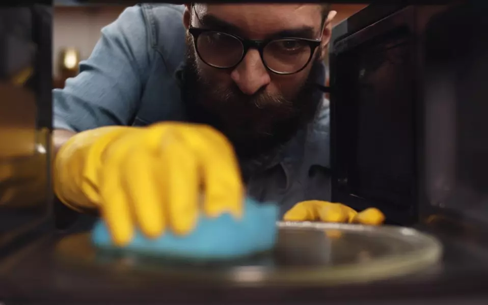चष्मा घातलेला दाढीवाला माणूस मायक्रोवेव्ह साफ करत आहे