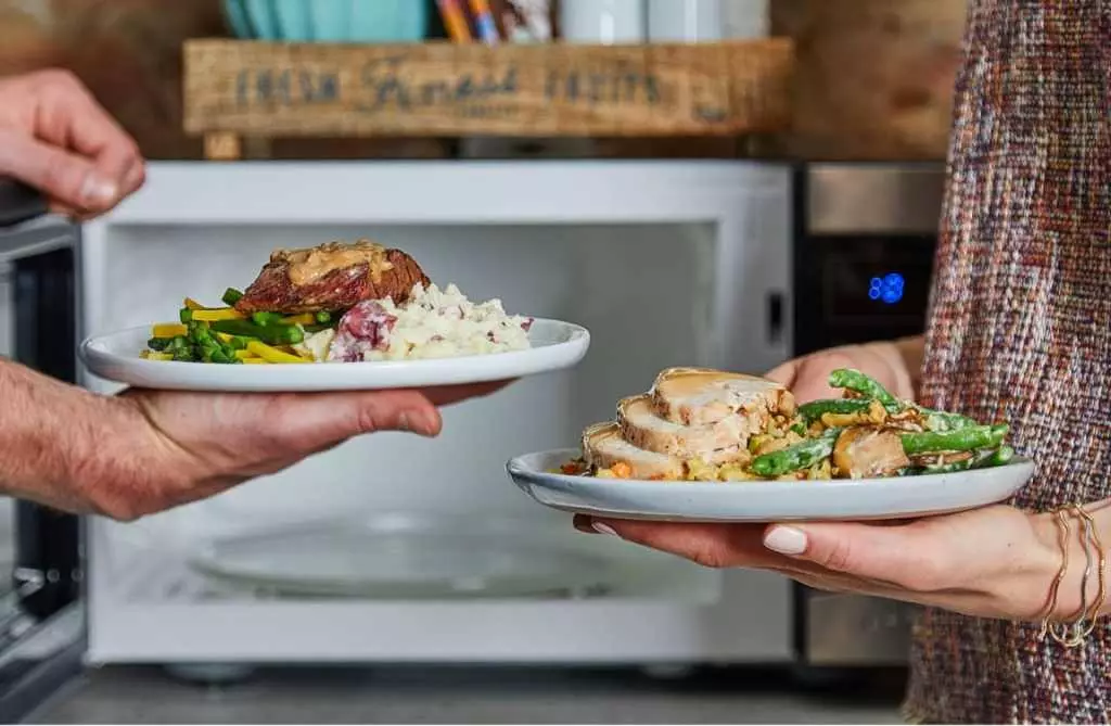 dúas persoas sostendo pratos de comida diante dun microondas