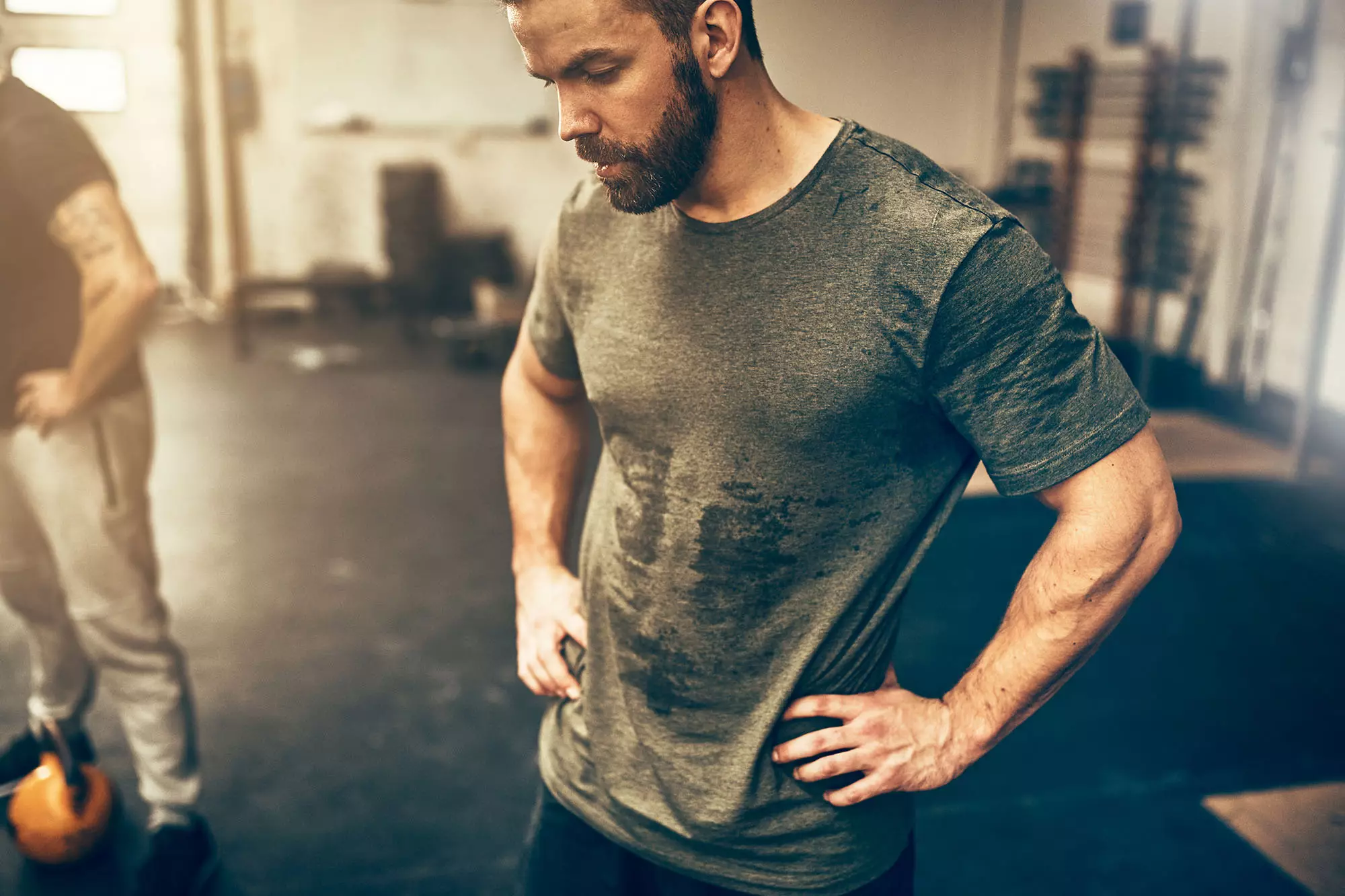 Un joven en forma con ropa deportiva de pie con las manos en las caderas en un gimnasio sudando después de una sesión de entrenamiento