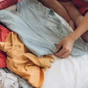 De mens vouwt en schikt de kleren op het bed nadat ze zijn gewassen.