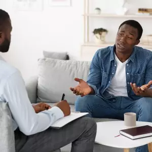 Lelaki kulit hitam yang tertekan menjelaskan masalahnya kepada ahli psikologi pada sesi terapi individu di pejabat, menyalin ruang