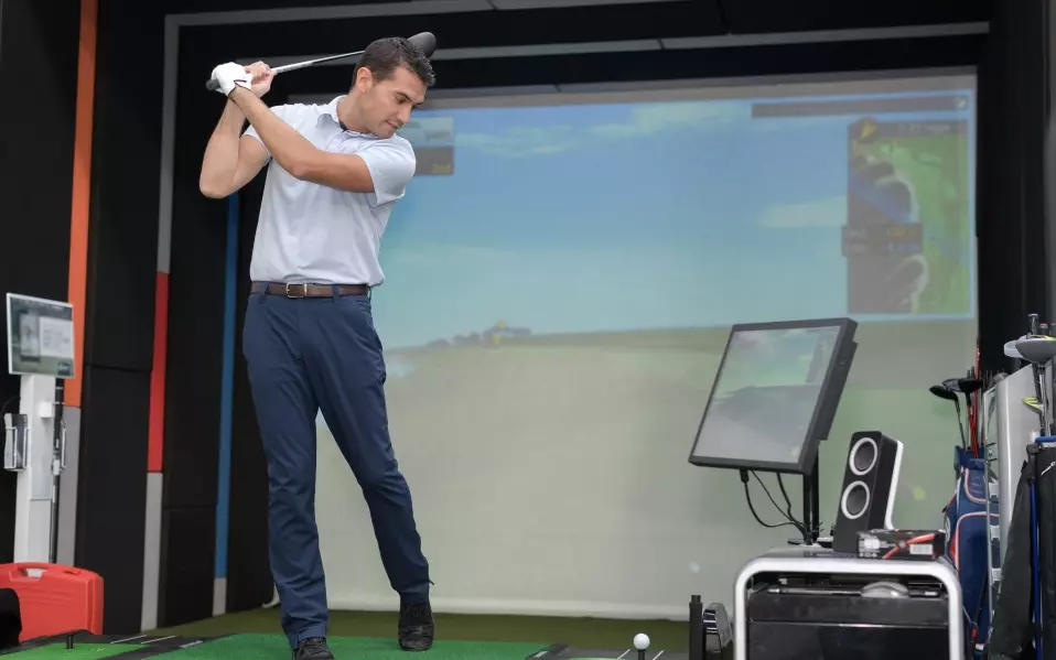 Мъж, практикуващ замах на голф с помощта на симулатор