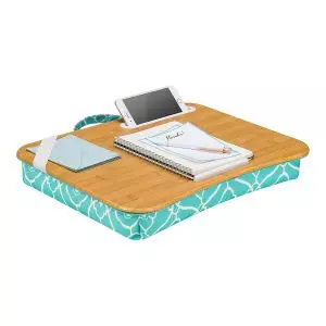 una mesa de bandeja de cama acolchada con lapgear de té que sostiene un cuaderno y un teléfono sentados en una superficie plana sobre un fondo blanco