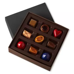 सफेद पृष्ठभूमि पर इसके ढक्कन के ऊपर नौ रंगीन चॉकलेट का एक डिब्बा